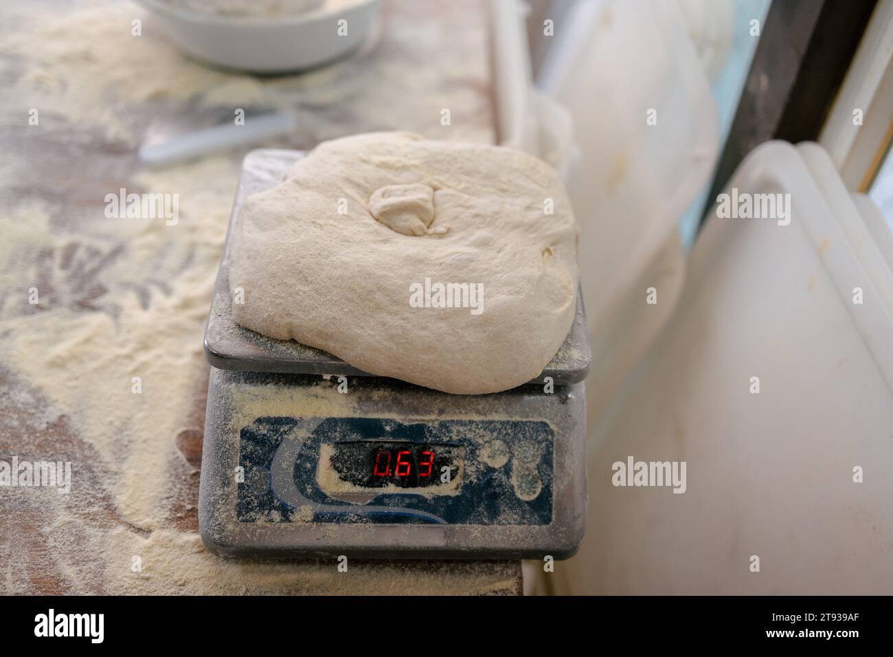 Detail shot of a bread dough being weighted on a scale in a table full ...