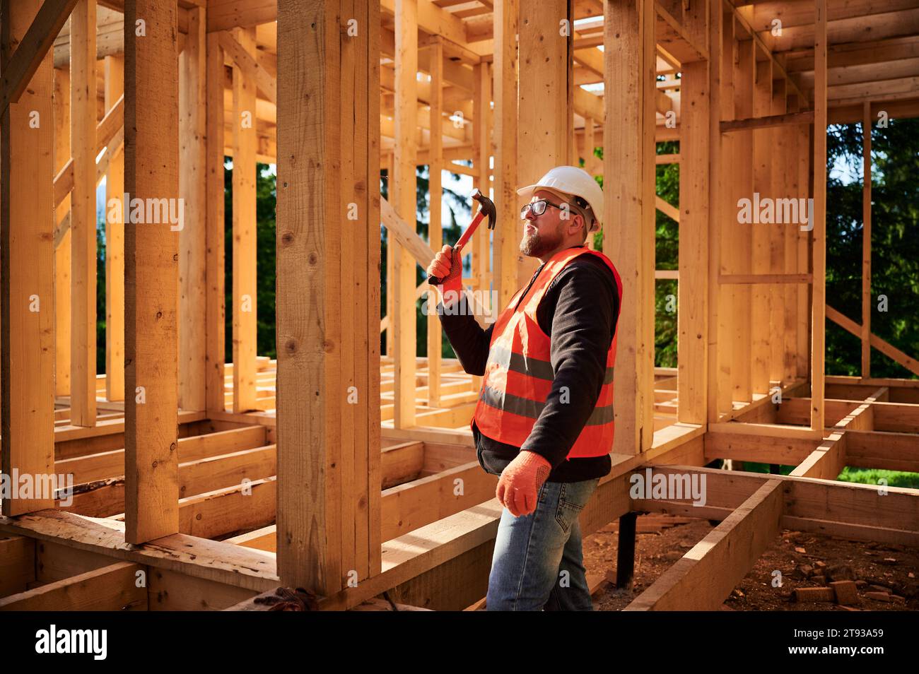 Carpenter constructing wooden frame house. Bearded man with glasses is ...