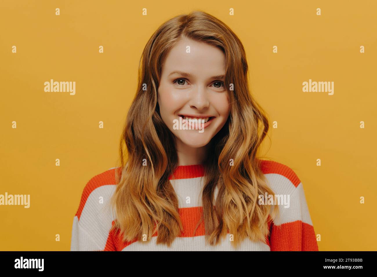 Brightly smiling woman with wavy hair in a striped sweater, exuding joy ...