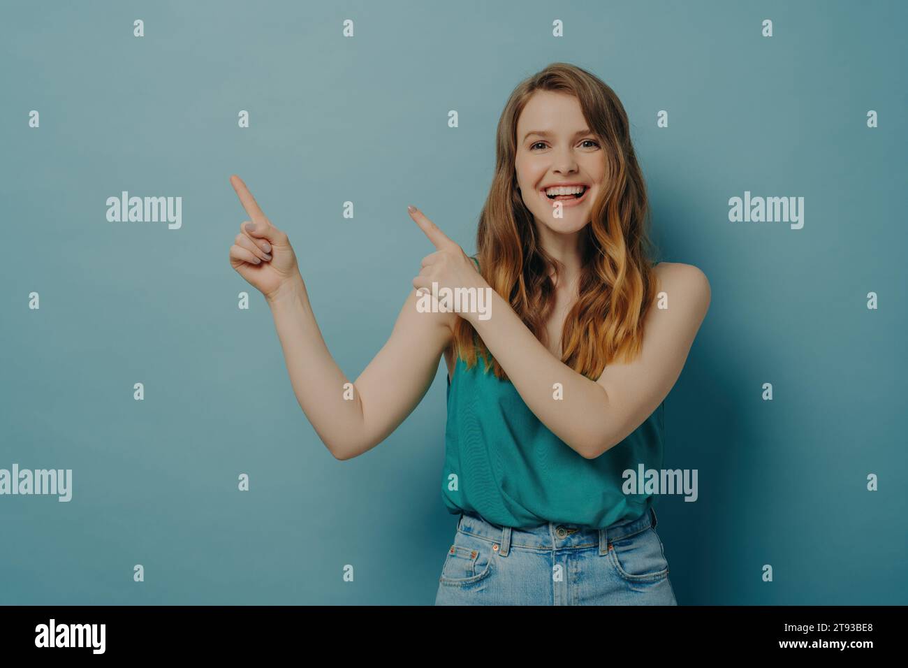 Joyful young woman pointing upwards with both hands, delighted ...