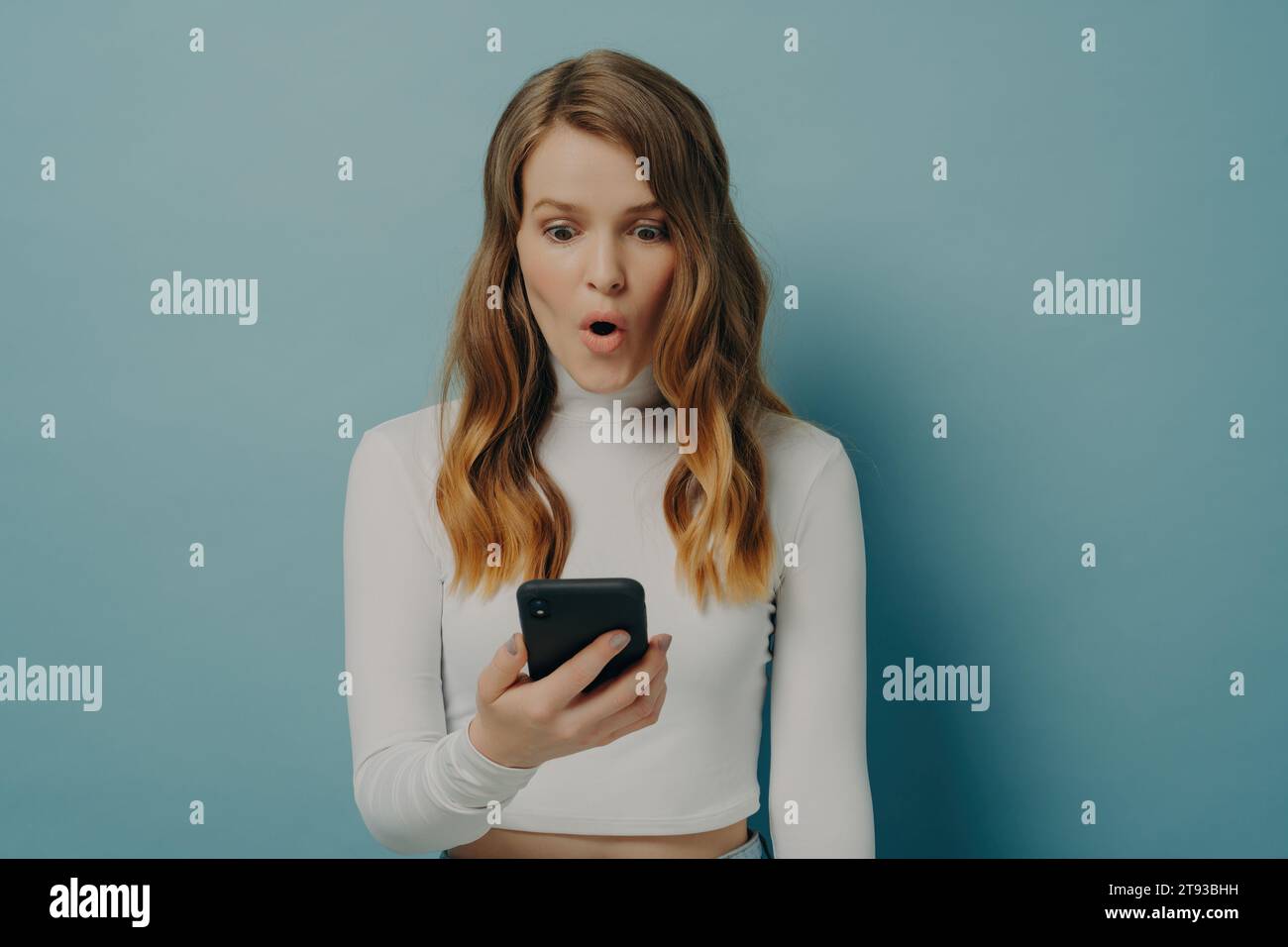 Shocked young woman holding phone, mouth agape, expressing surprise ...