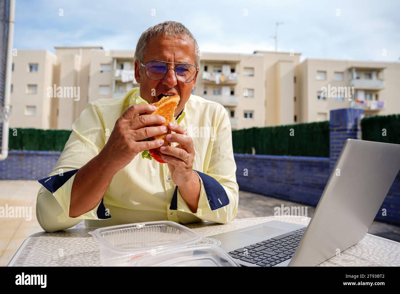 Businessperson wearing suit eating a sandwich working on a terrace ...