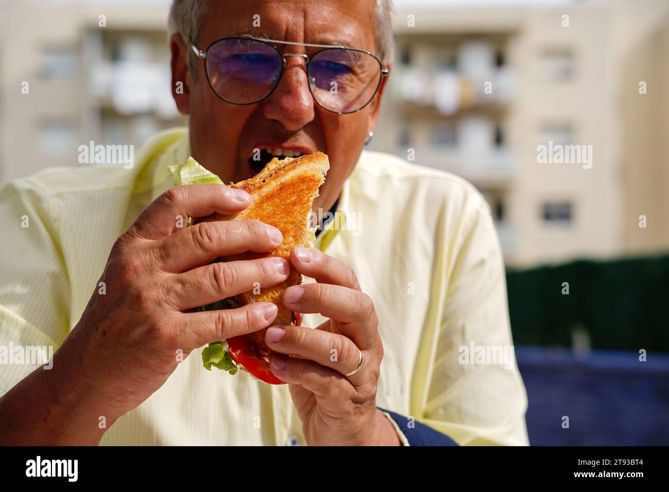 Businessperson in a suit eating a sandwich working on a terrace. Lunch ...
