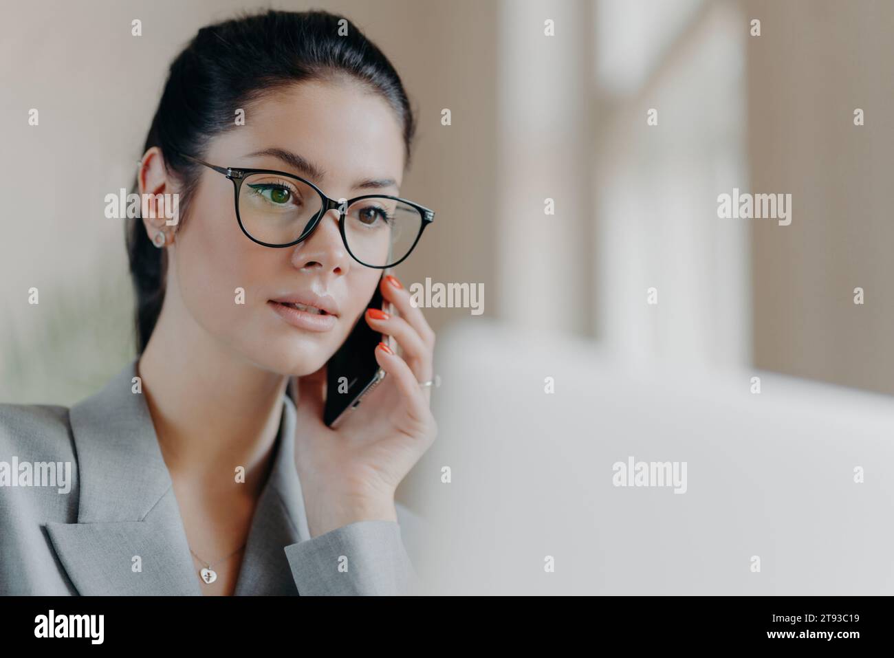 Focused secretary in glasses speaking on the phone in a modern office ...