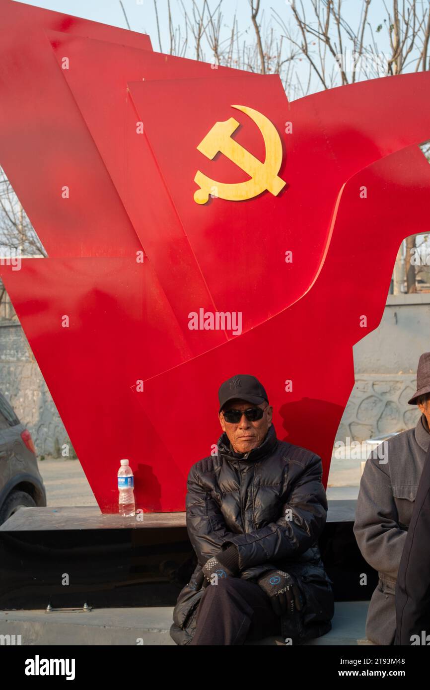 Elderly people sit in front of a sculpture of a red flag with the logo ...
