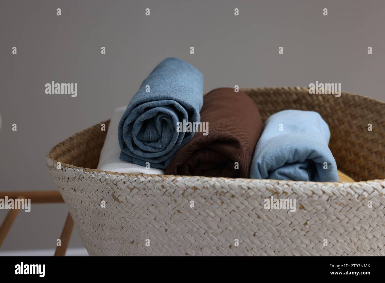 Different rolled clothes in basket against grey wall, closeup ...