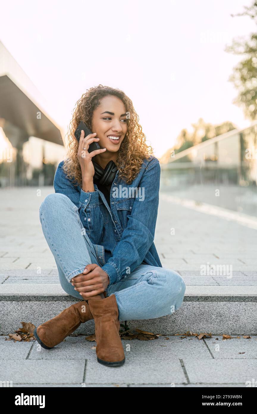Full body of cheerful female in denim jacket and jeans speaking on ...