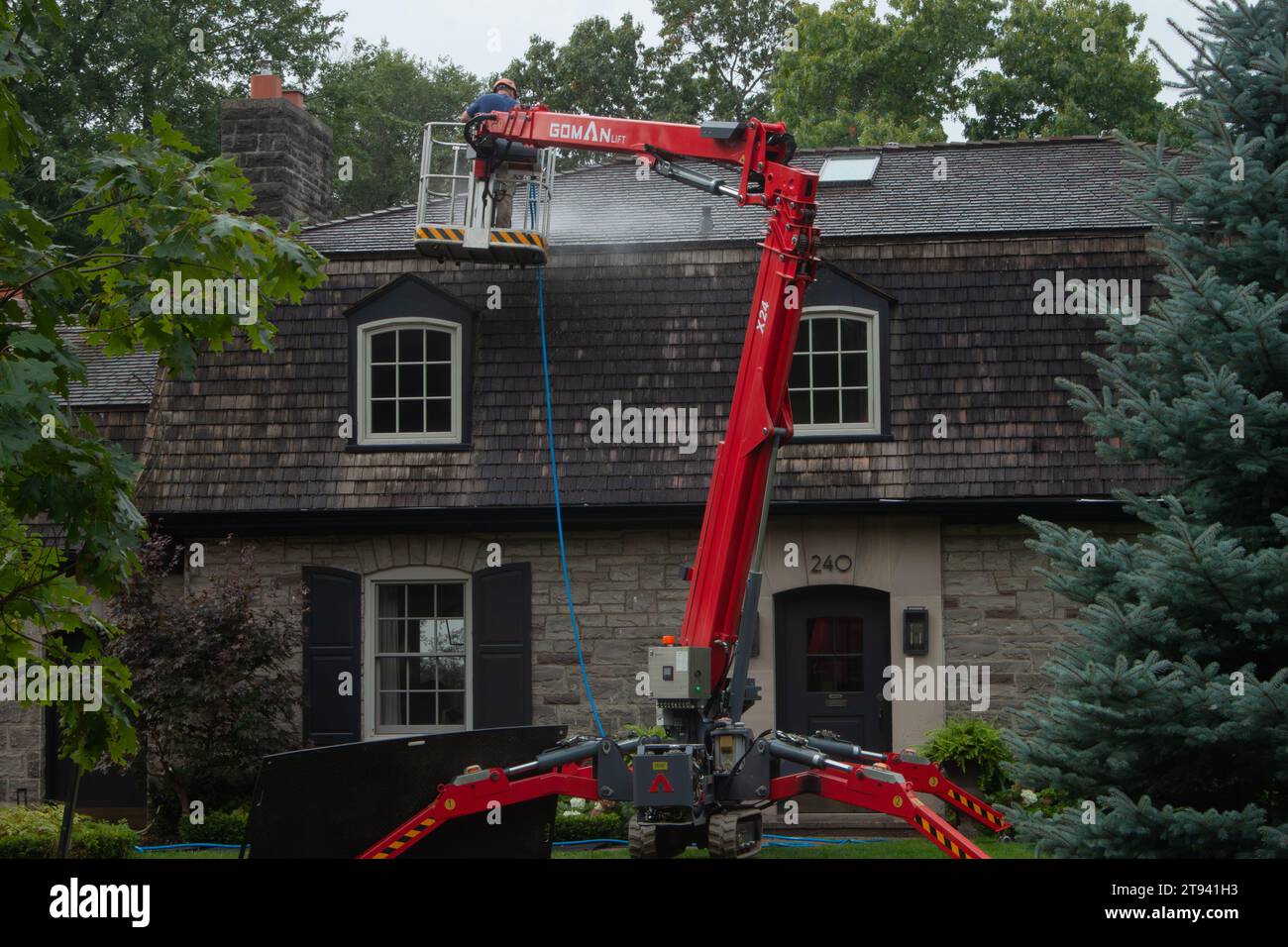 Roof cleaning, worker hard at work using a pressure washer to clean a ...