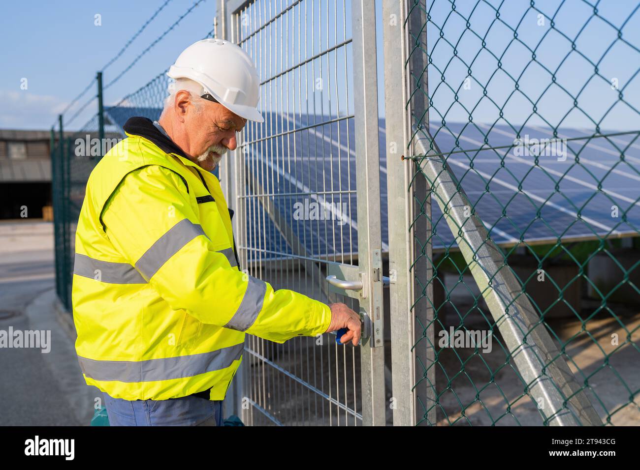 Electrical engineer in safety gear opening a gate to a solar field ...