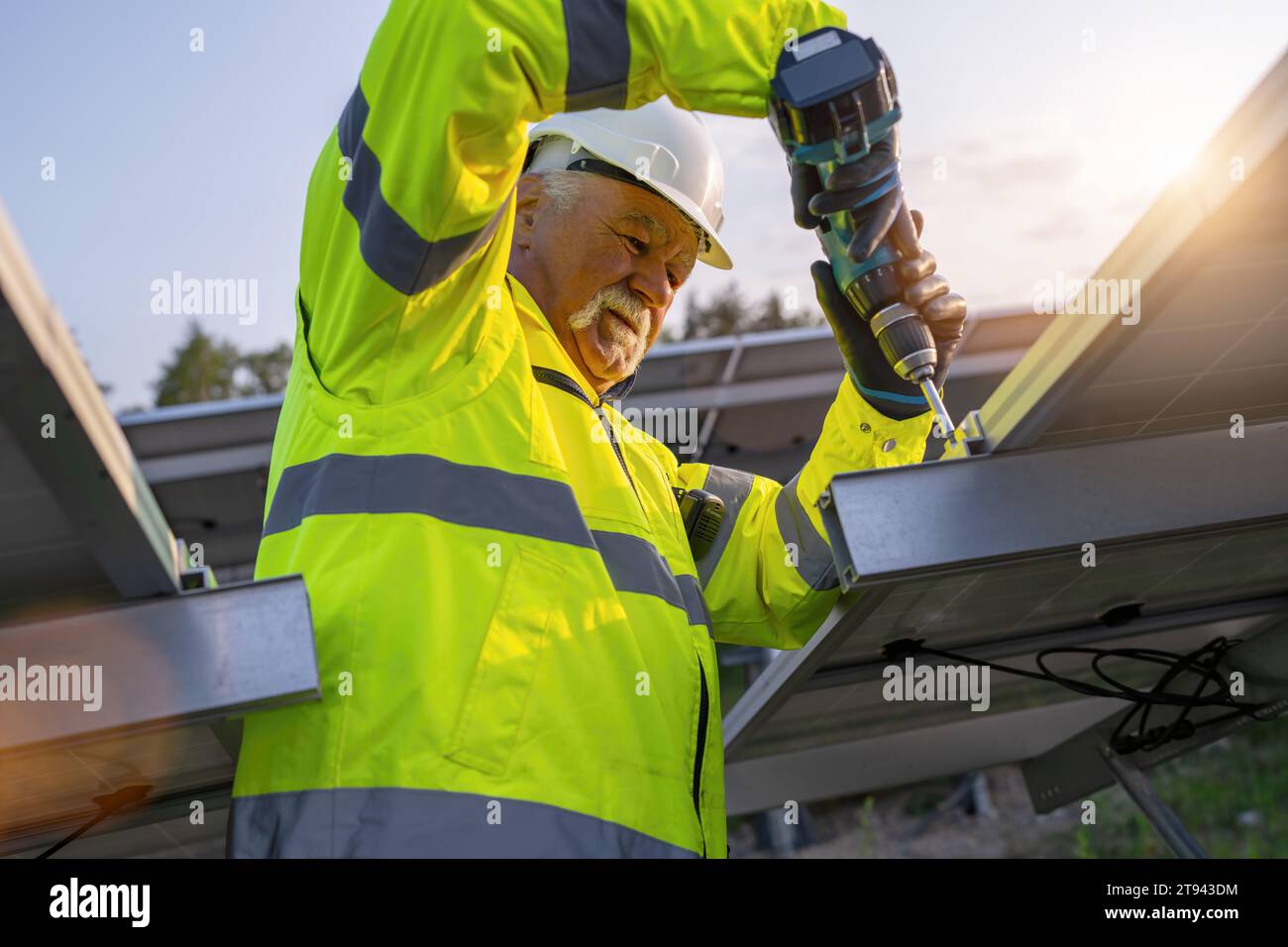 Engineer using a cordless drill to install solar panels at dawn ...