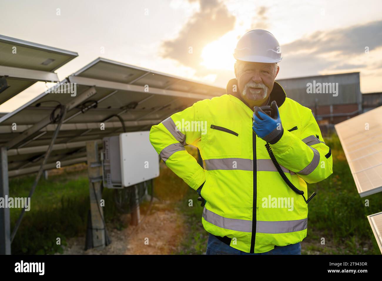 Smiling engineer communicating with a walkie-talkie at a solar power ...
