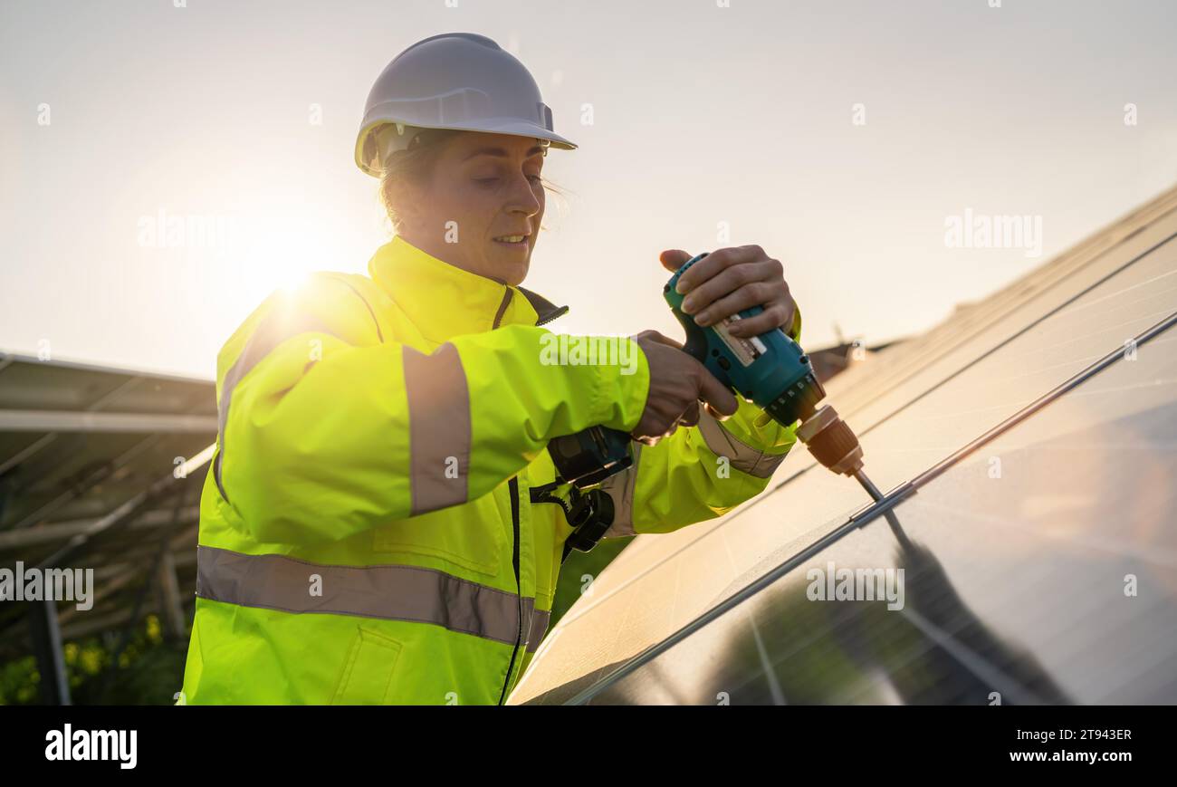 Technician assembling solar panels with a cordless drill at sunset ...