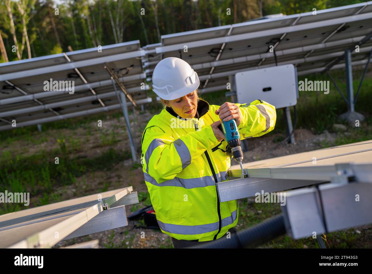 Female technician using a cordless drill on solar panel structure in a ...
