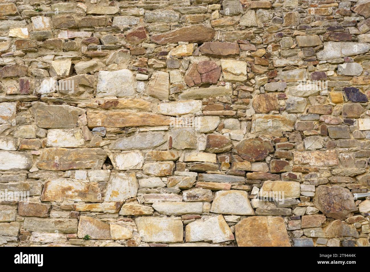 Old rough stone wall made of various square natural stones in beige ...