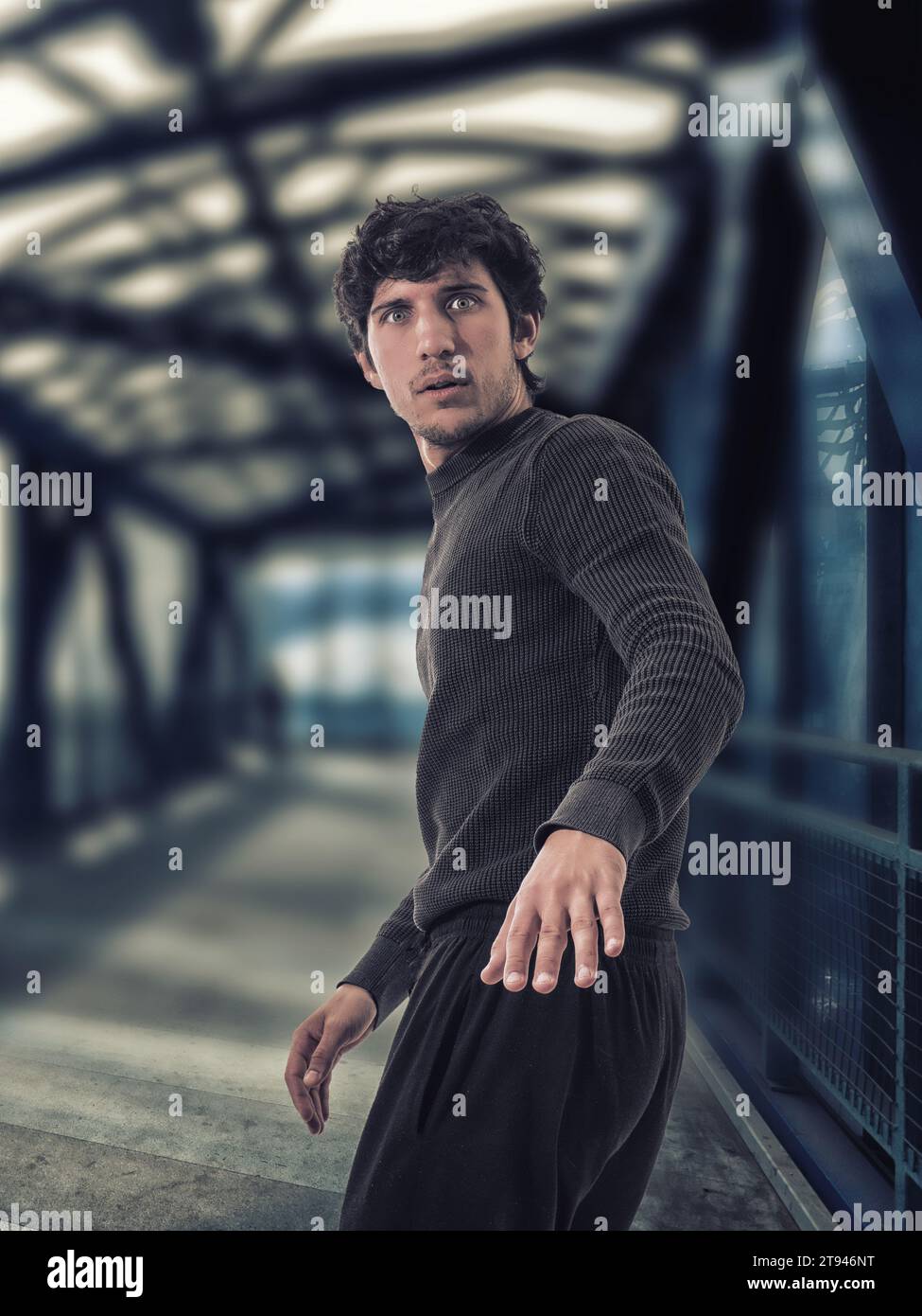 A young man standing on a bridge, running away looking scared or ...