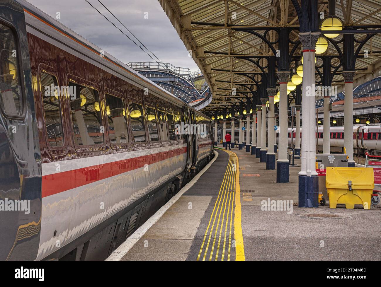 A railway carriage stands at a station platform where the lights of a ...