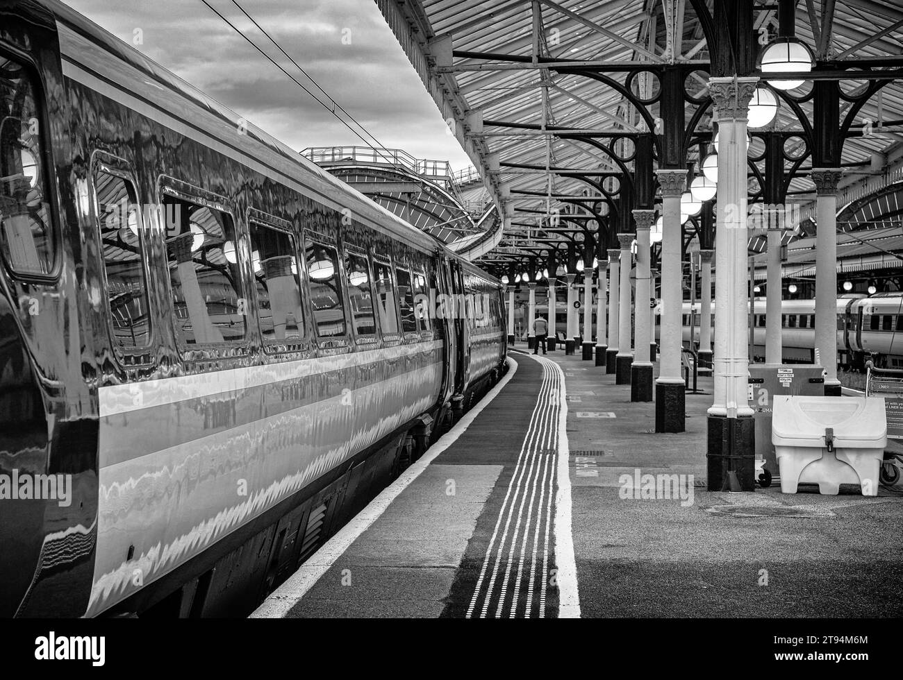 A railway carriage stands at a station platform where the lights of a ...