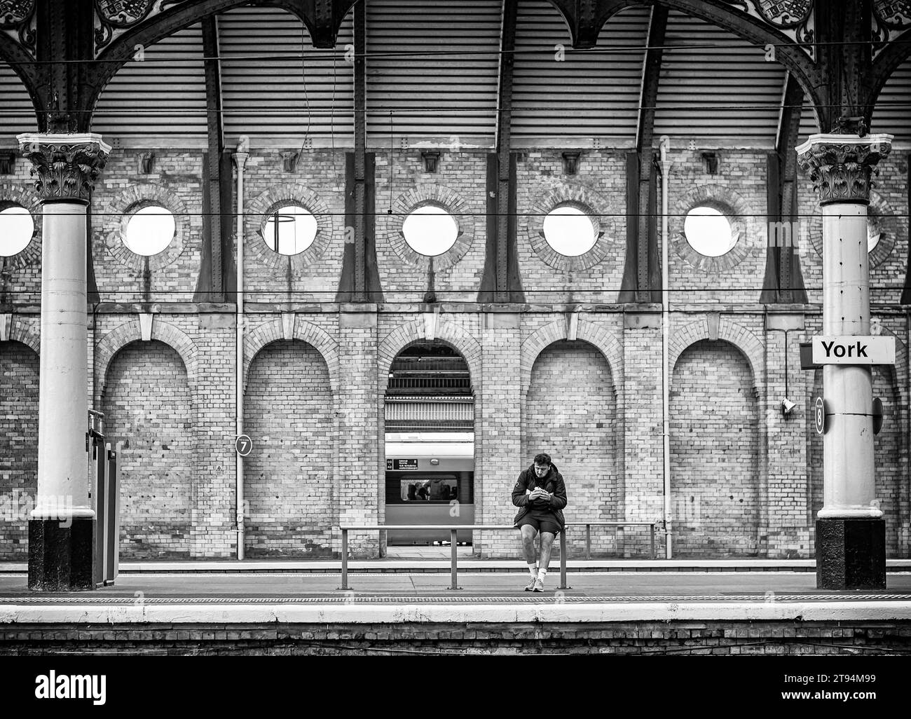 A man sits on a bench in a railway station between two historic columns ...