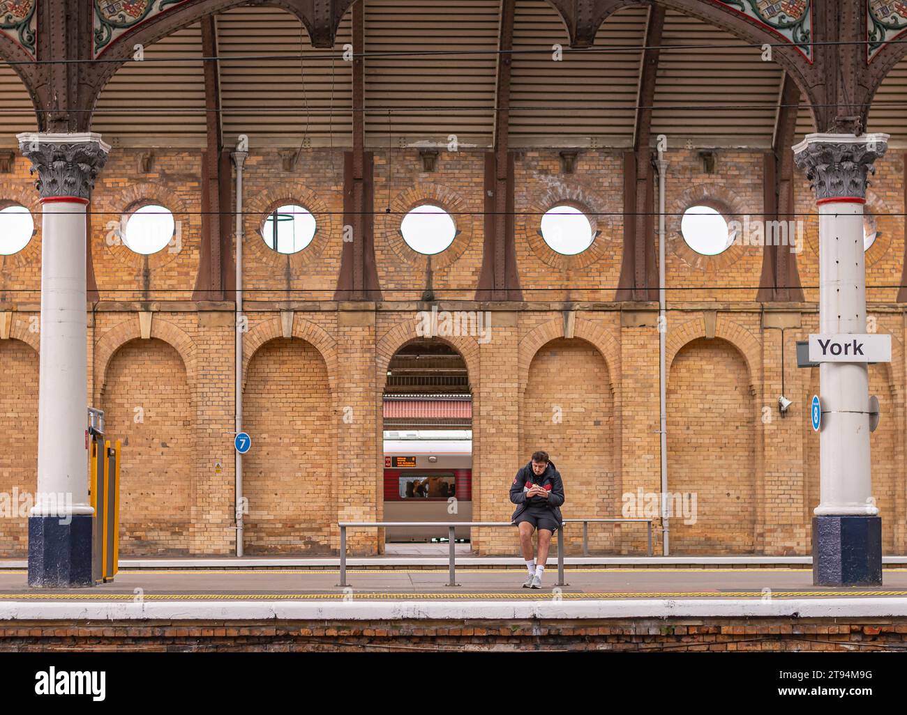 A man sits on a bench in a railway station between two historic columns ...