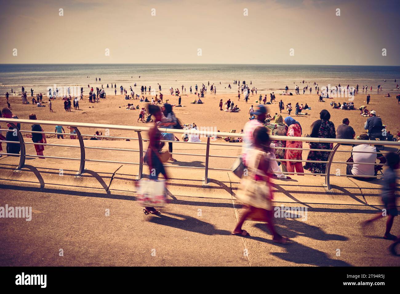 Blurred figures of tourists walking down ramp to the beach in summer ...