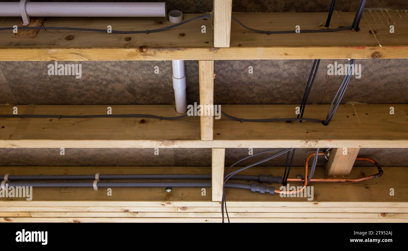 Under floor view showing various pipes and cables in a wooden beam ...