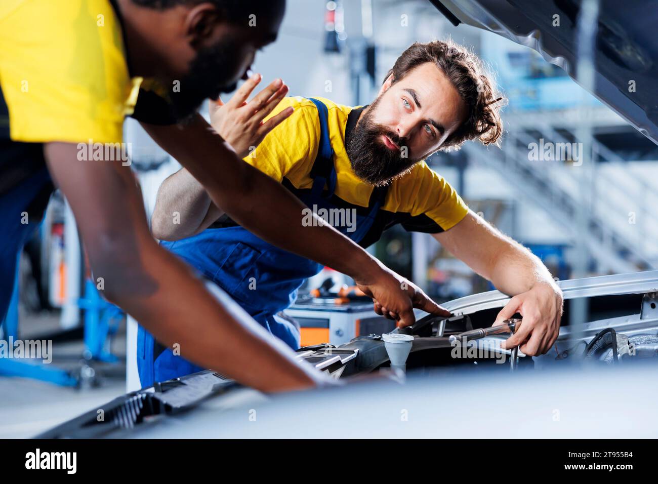 Colleagues in car service using professional mechanical tool to repair ...