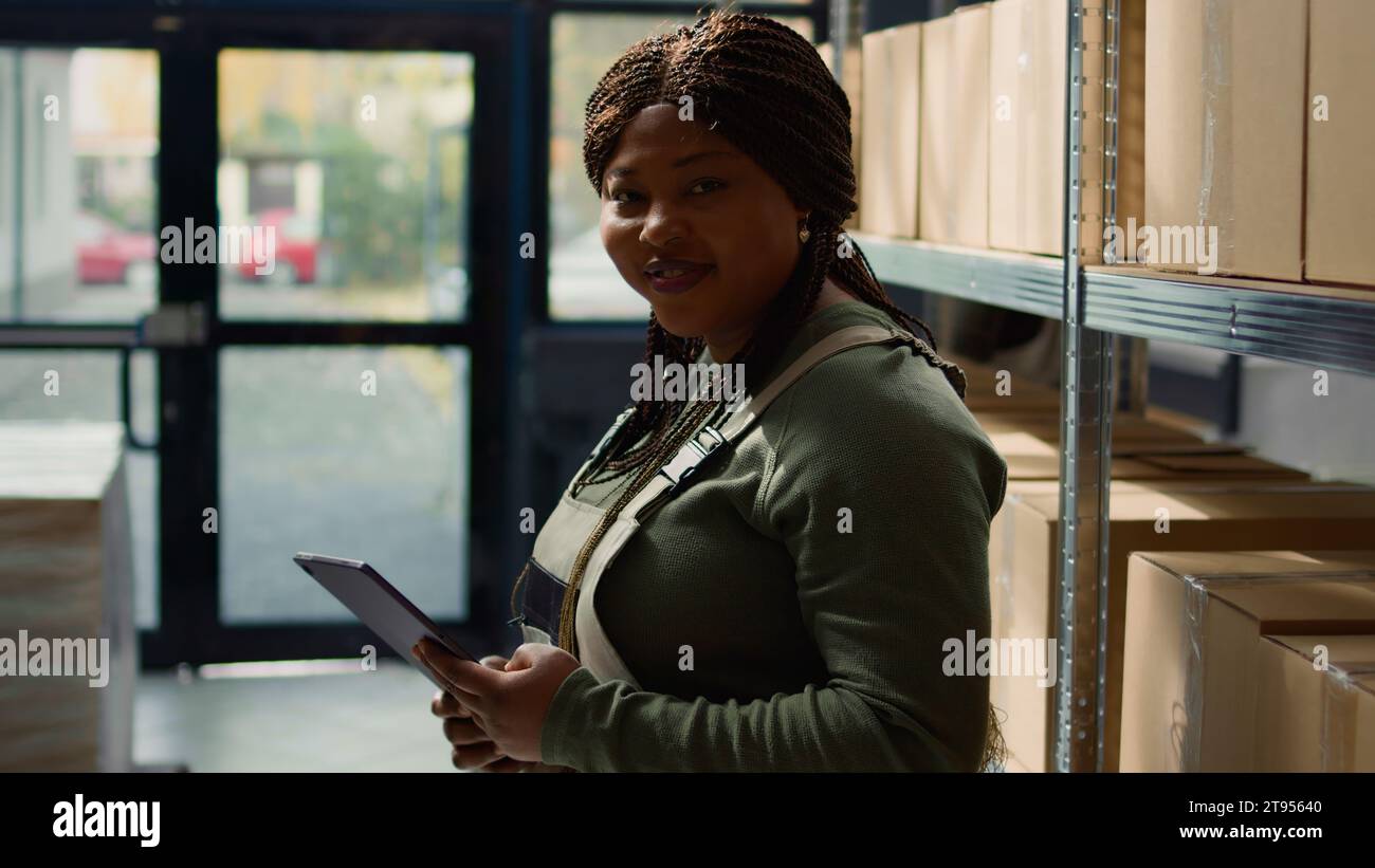 Portrait of joyful warehouse supervisor holding tablet, standing in ...