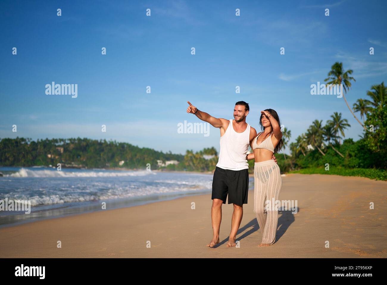 Happy couple enjoying romantic walk on tropical beach, man pointing ...