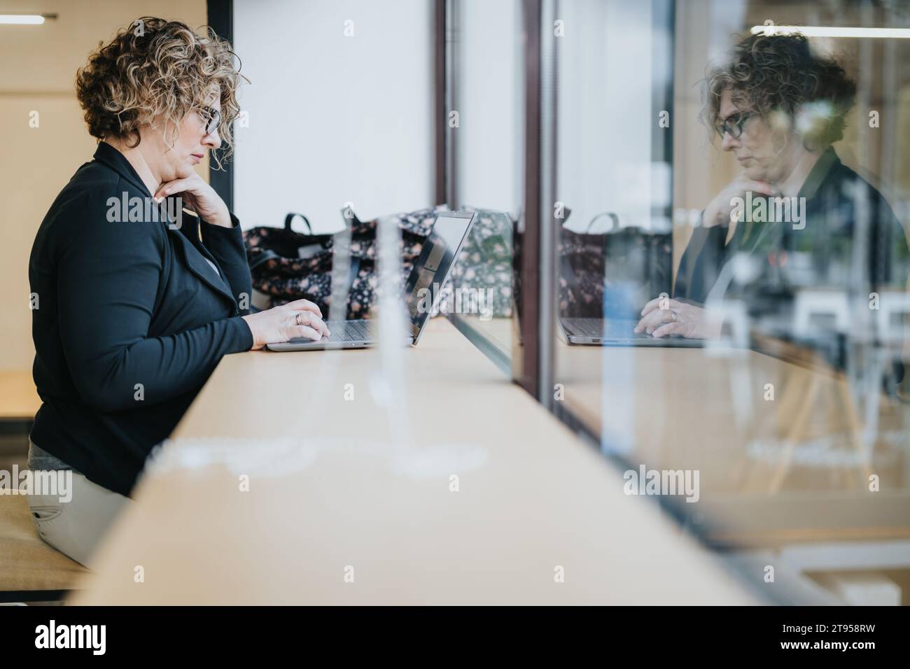 Middle-aged businesswoman sitting at working desk next to the window ...