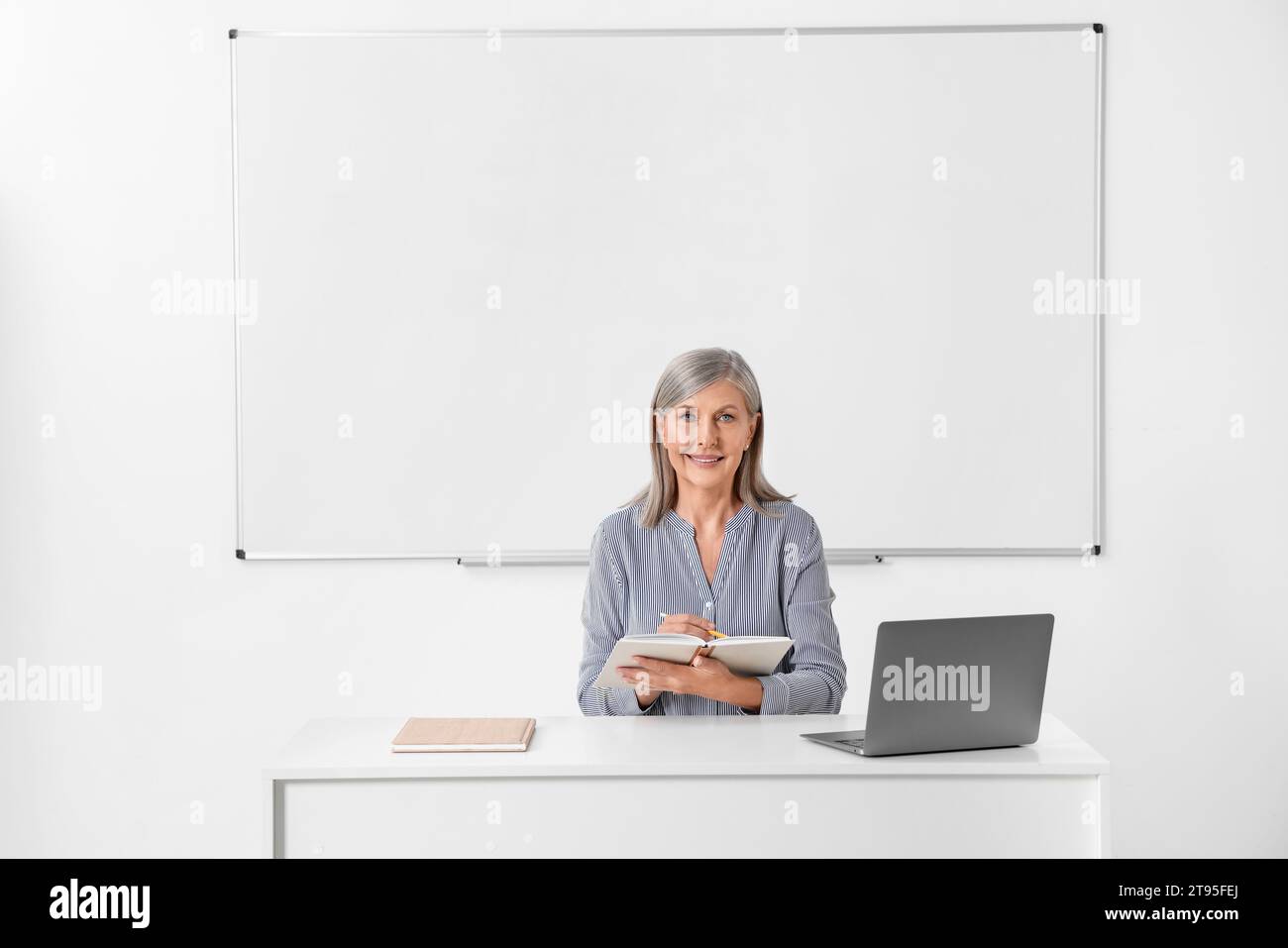 Happy professor giving lecture near laptop at desk in classroom, space ...