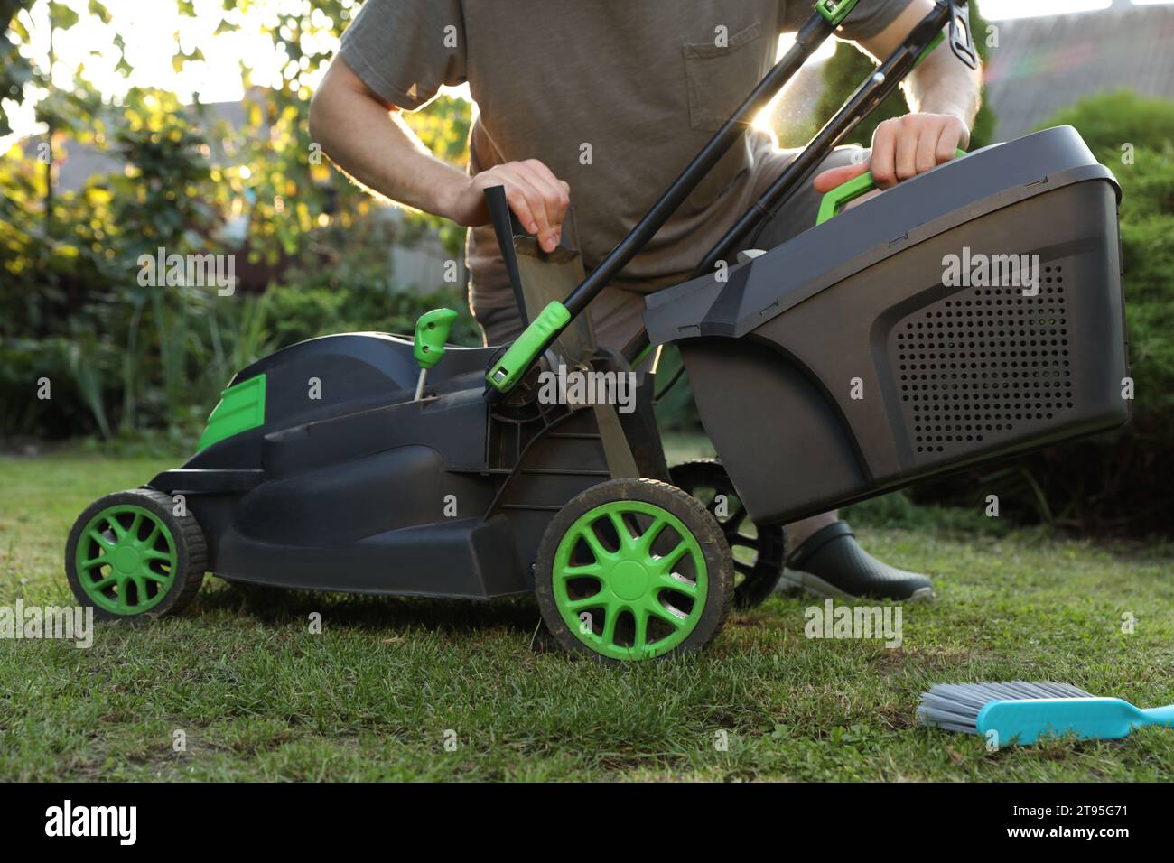 Cleaning lawn mower. Man detaching grass catcher from device in garden ...