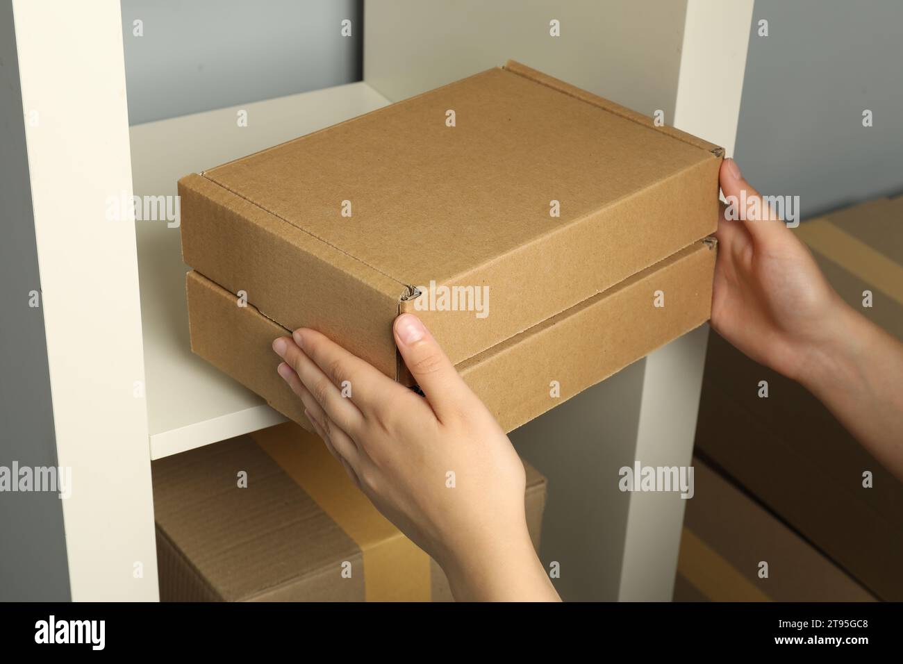 Woman putting cardboard box on shelf indoors, closeup. Packaging goods ...