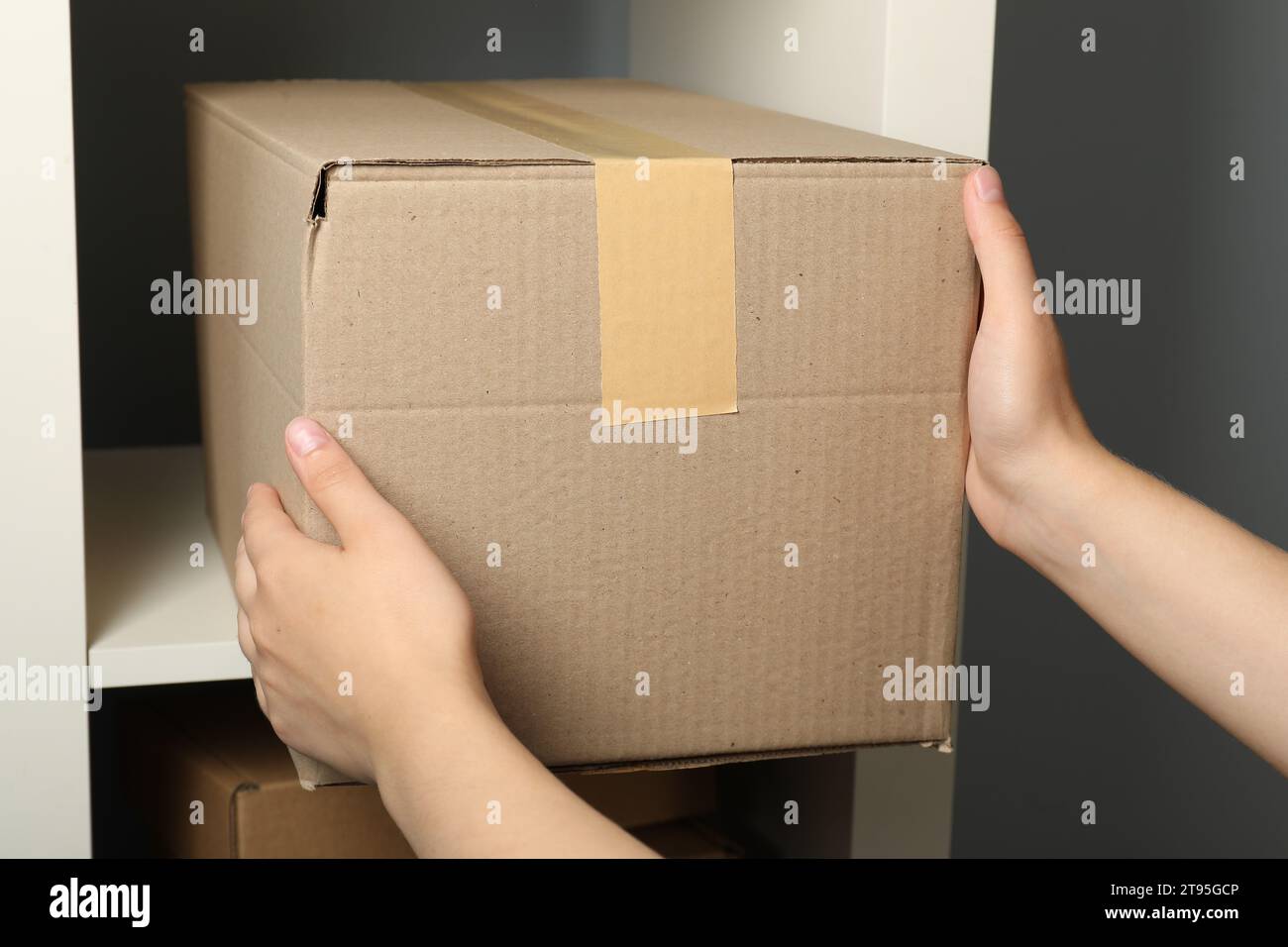 Woman putting cardboard box on shelf, closeup. Packaging goods Stock ...