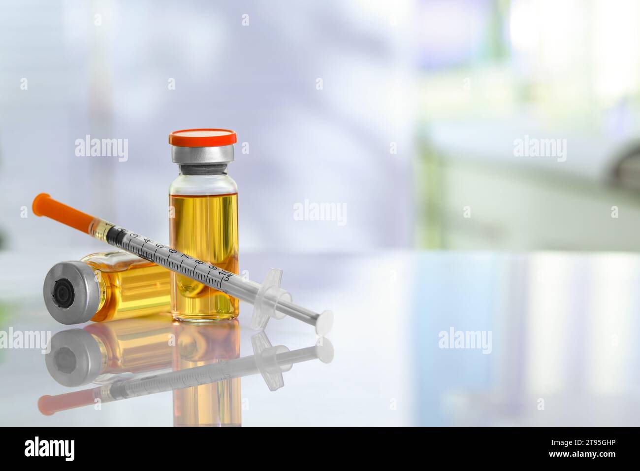 Glass vials and syringe with orange medication on white table. Space ...