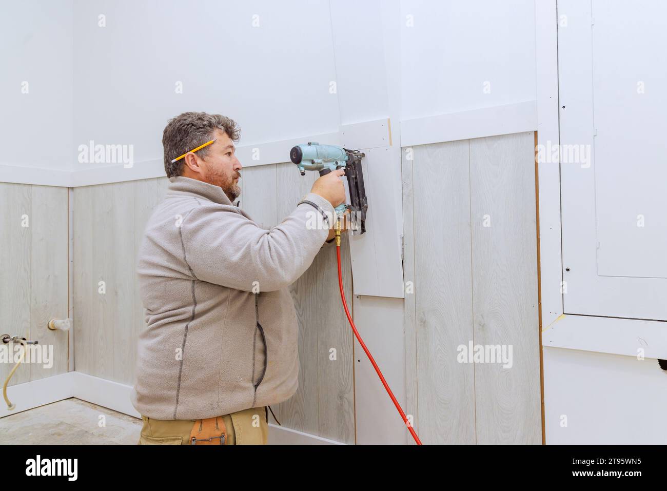 There is worker from contractor nailing wooden trim moldings on walls ...