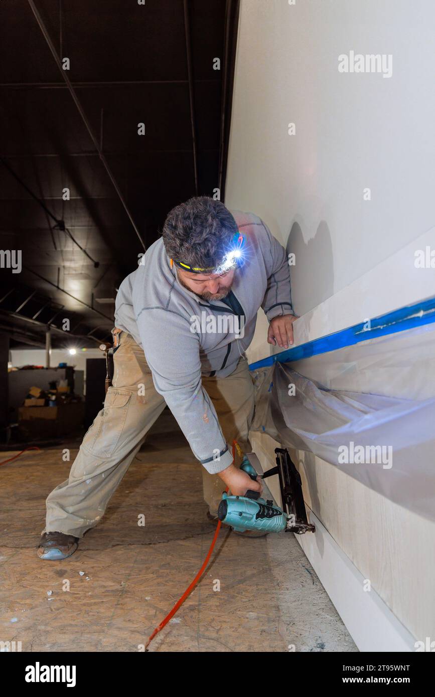 Contractor nails wooden trim moldings in room during installation of ...