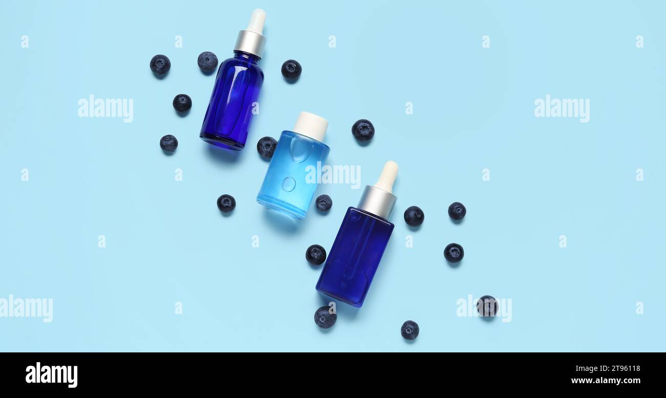Bottles of cosmetic products and blueberry on light blue background ...