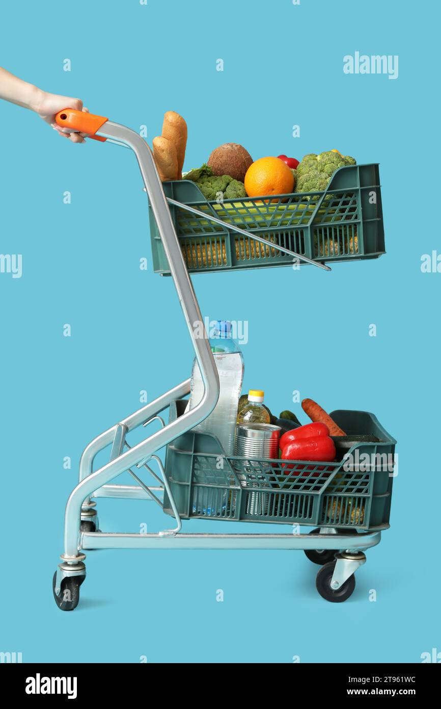 Woman pushing shopping cart full of food on blue background Stock Photo ...