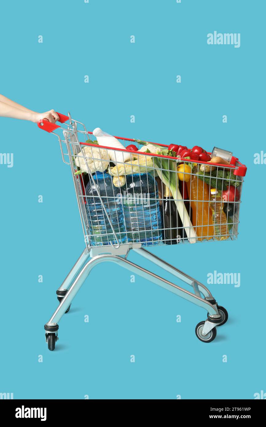 Woman pushing shopping cart full of food on blue background Stock Photo ...