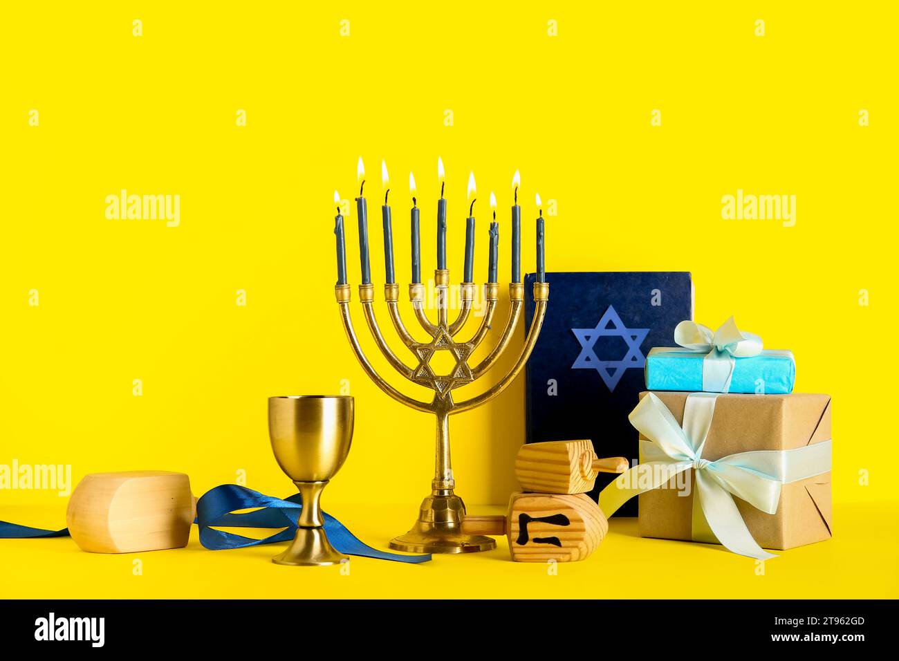 Menorah with Torah, gift boxes, dreidels and cup on yellow background ...