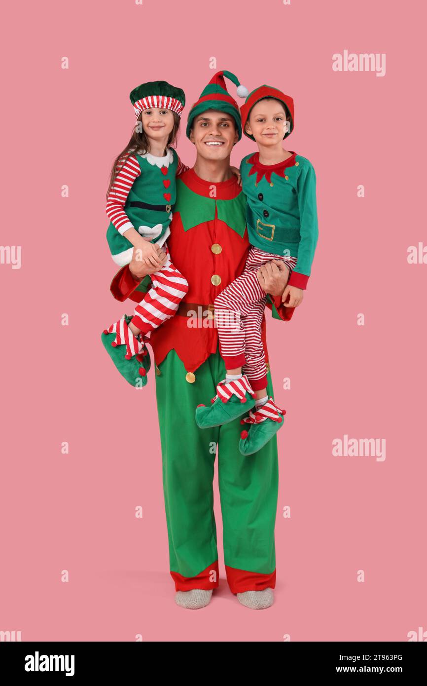 Father and cute little children in elf's costumes on pink background ...