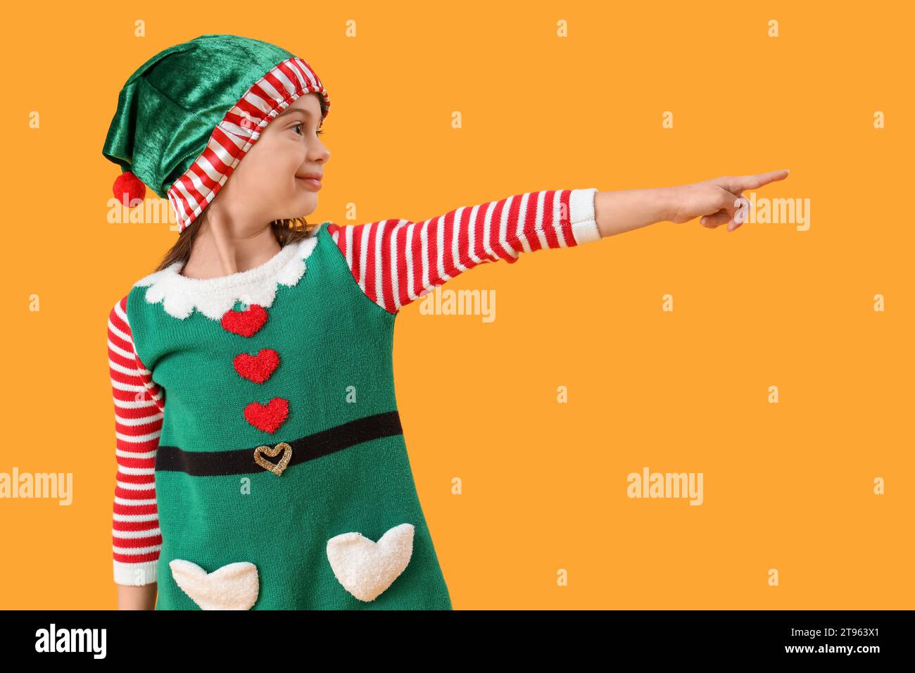 Cute little girl in elf's costume pointing at something on yellow ...