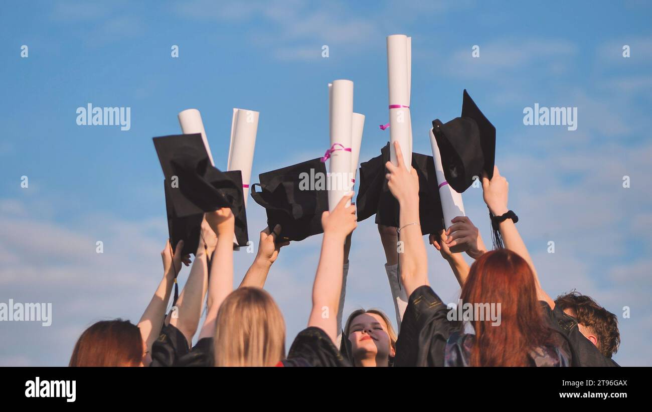 College graduates raise their hands with caps and diplomas to the sky ...
