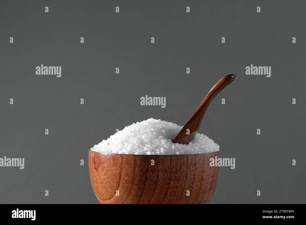 White table salt granules falling into a pile. Wood bowl. Gray color ...