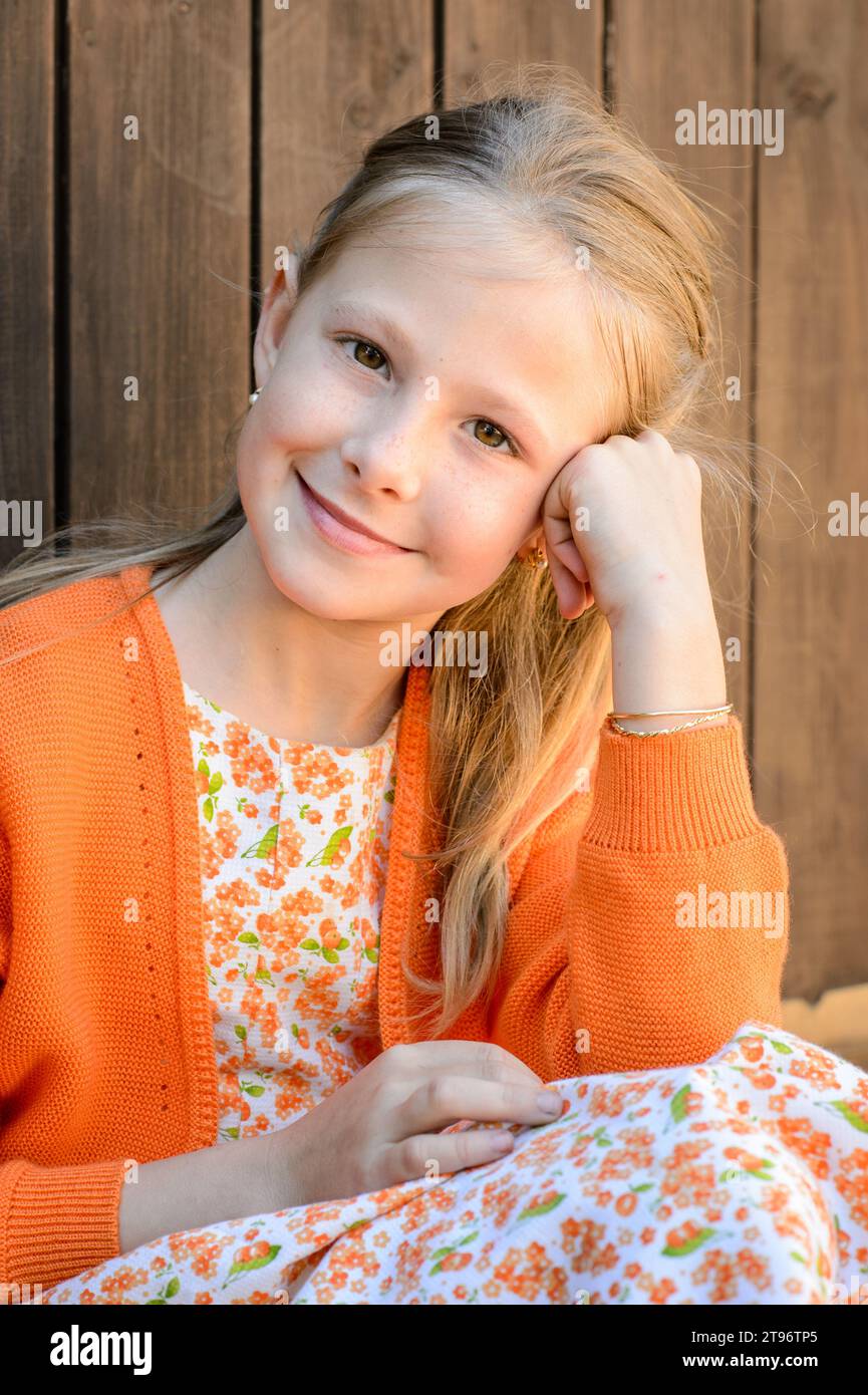Tender child in orange wear with floral ornament looking at camera with ...