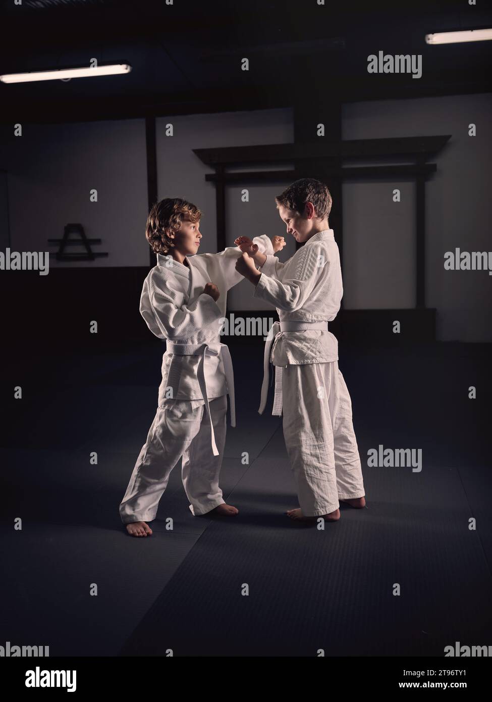 Side view of kids in white costume practicing punch and defence in judo ...