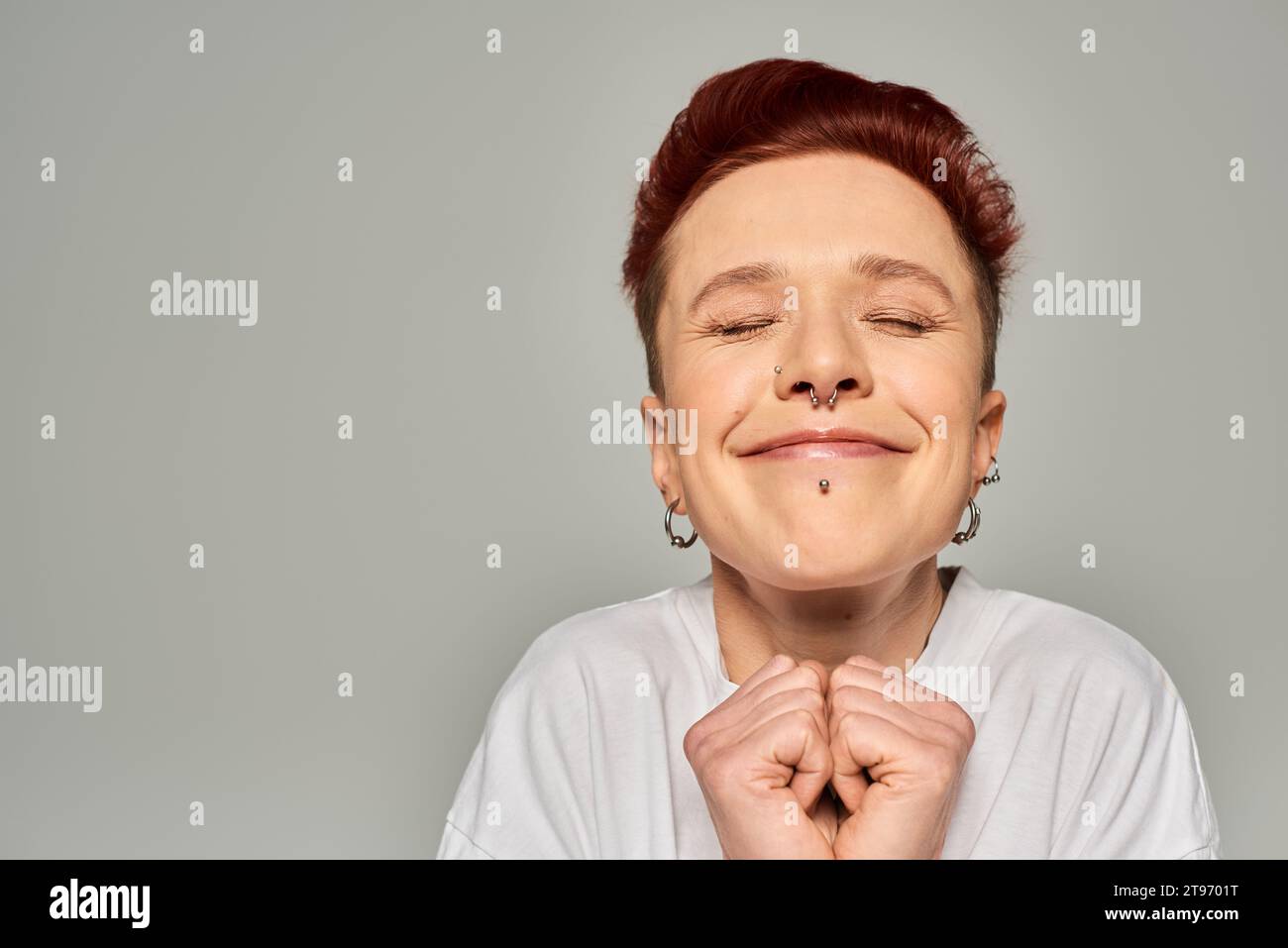 excited redhead bigender person with facial piercing smiling with ...