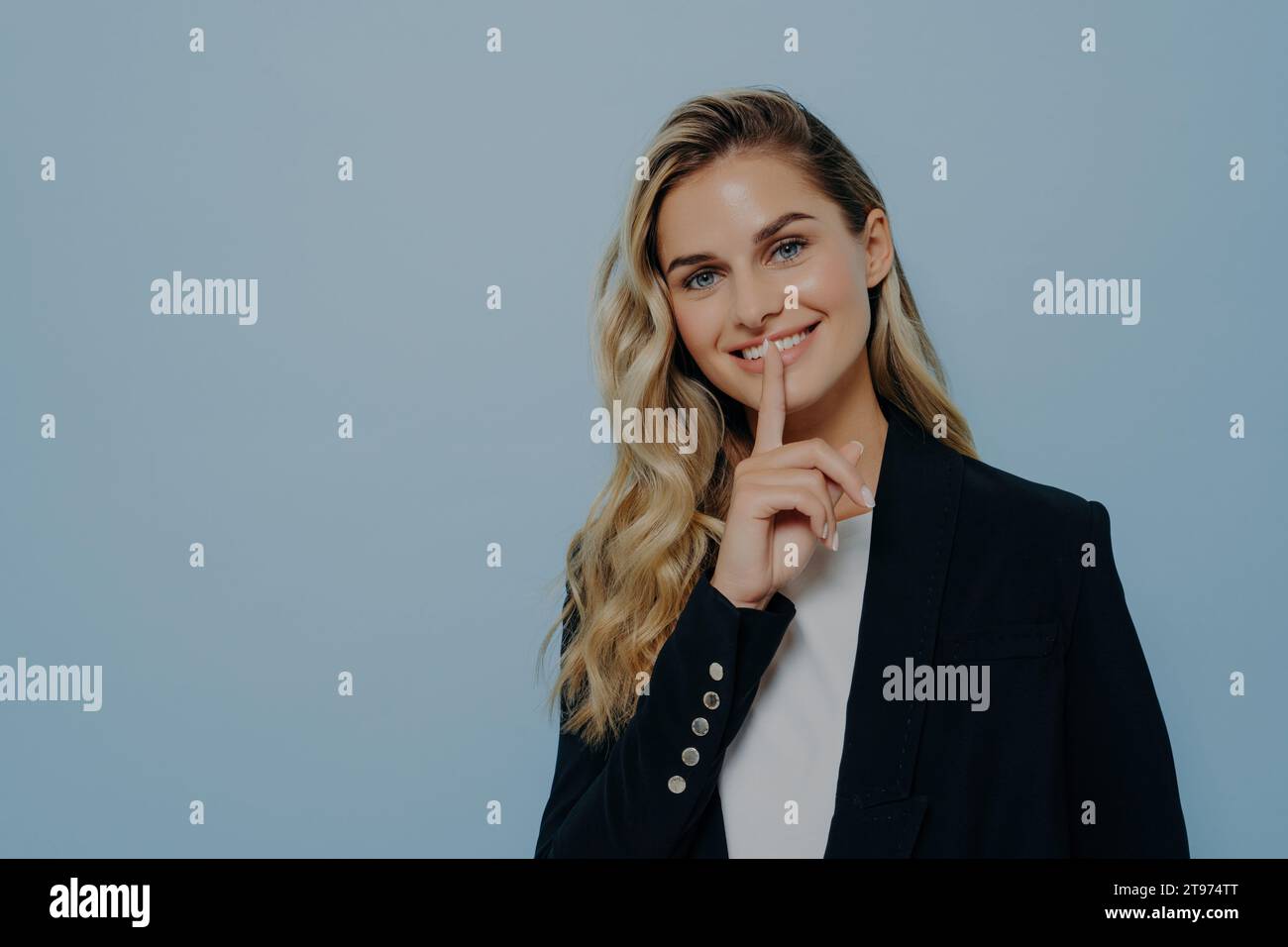 Stylish woman in black blazer, finger to lips, secret smile, blue ...
