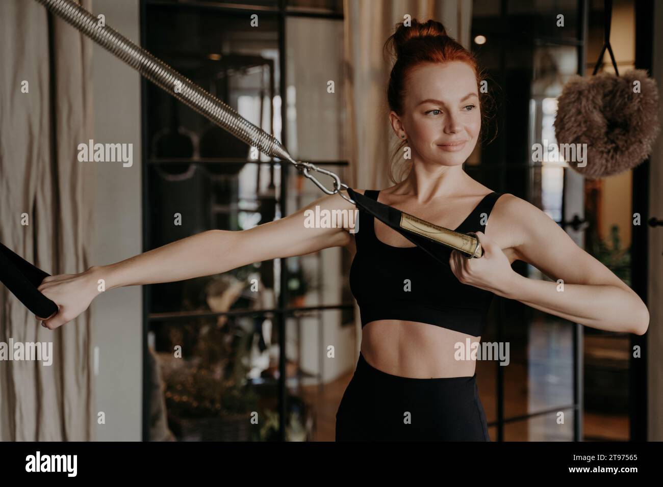 Focused Redhead Woman Exercising On A Cable Machine In A Gym Displaying Dedication And A Fit