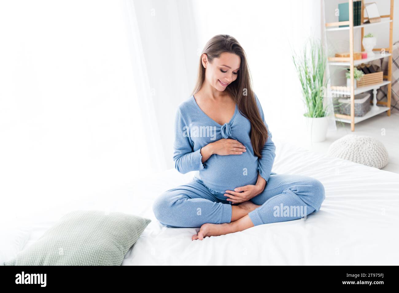 Photo of cute sweet gentle mom sitting in bed touching belly enjoying nice moment motherhood ...